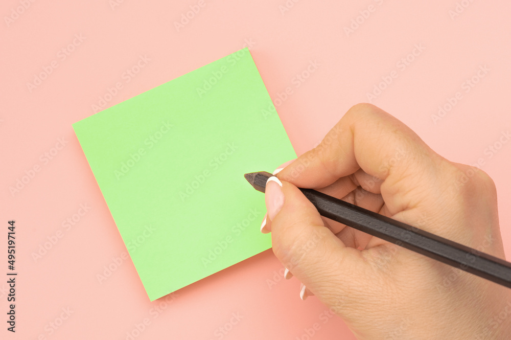 Hand written notes black pencil on green sticker. pink table background ...