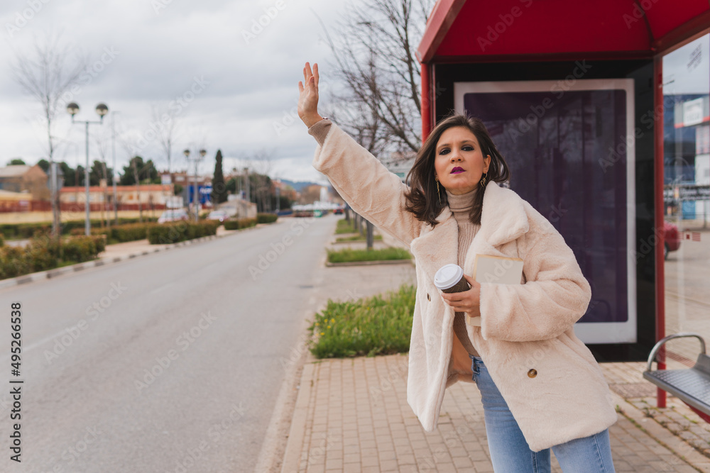 Young woman raising her hand to make the stop signal to the bus that ...