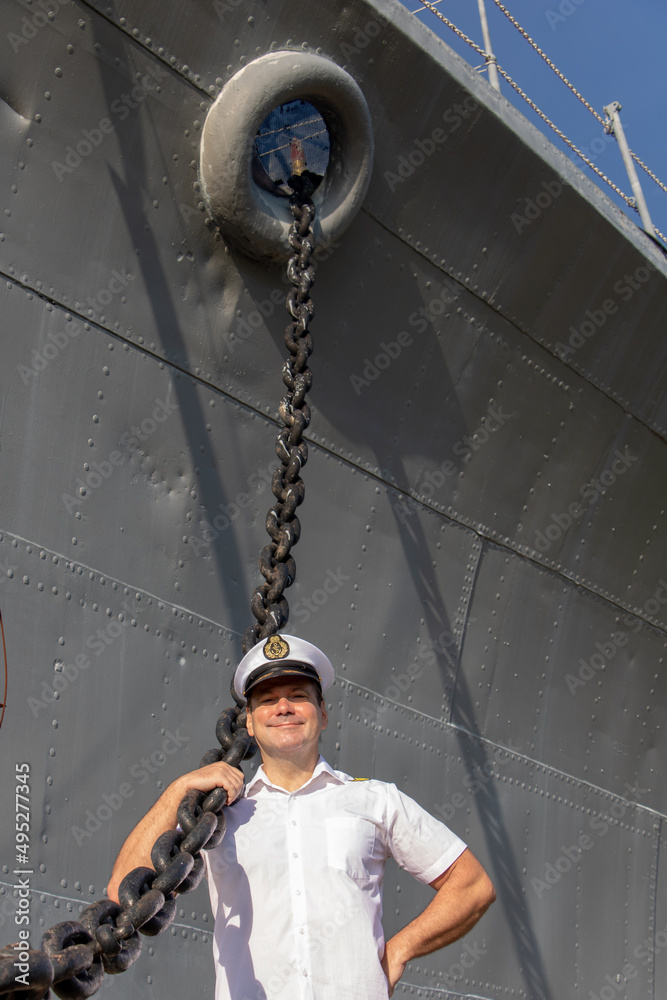 Naval officer in white uniform holding an anchor chain under a warship ...