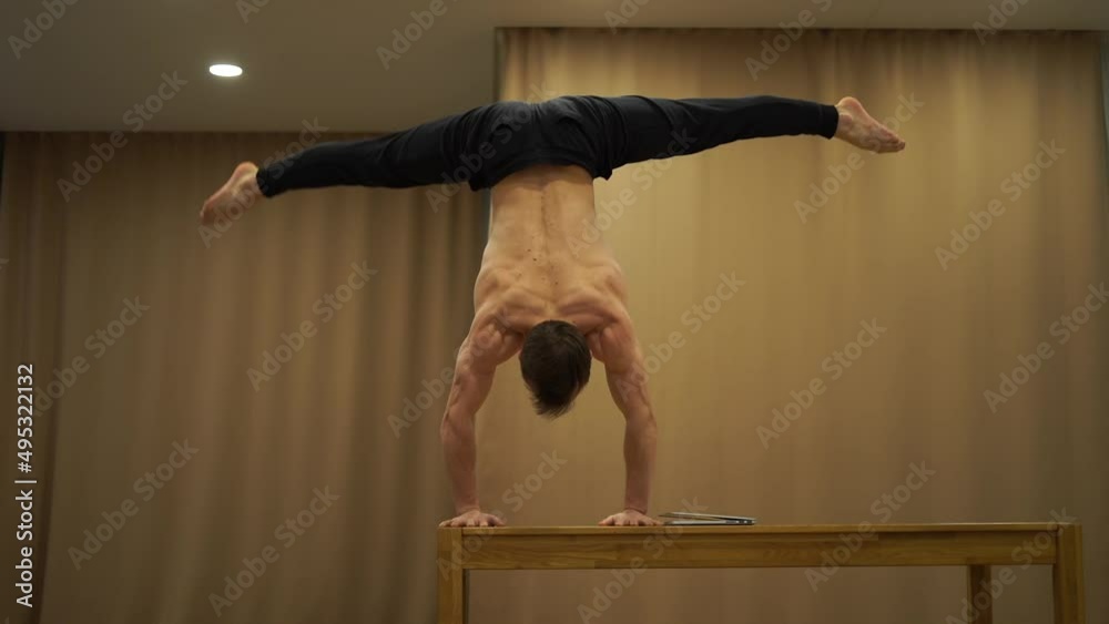 A muscular man keeps balance on one hand and uses laptop. Concept of ...
