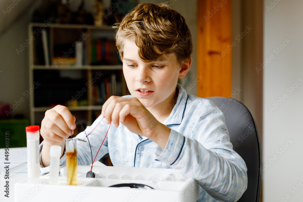 Preteen kid boy doing electric physical experiment as homework at home ...