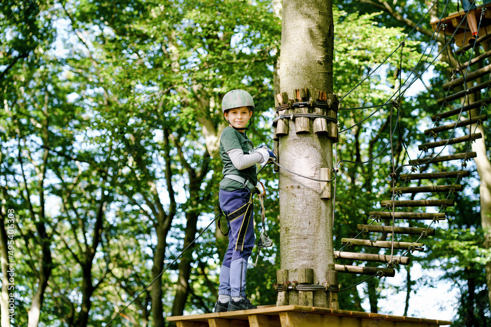 School boy in forest adventure park. Acitve child, kid in helmet climbs ...