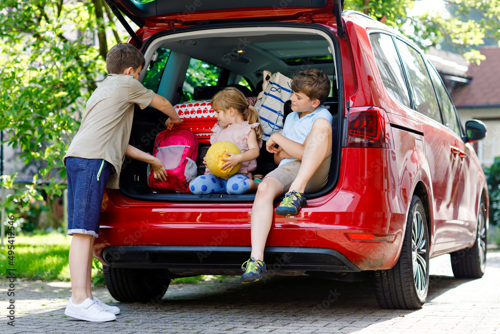 Three children, two boys and preschool girl sitting in car trunk before ...