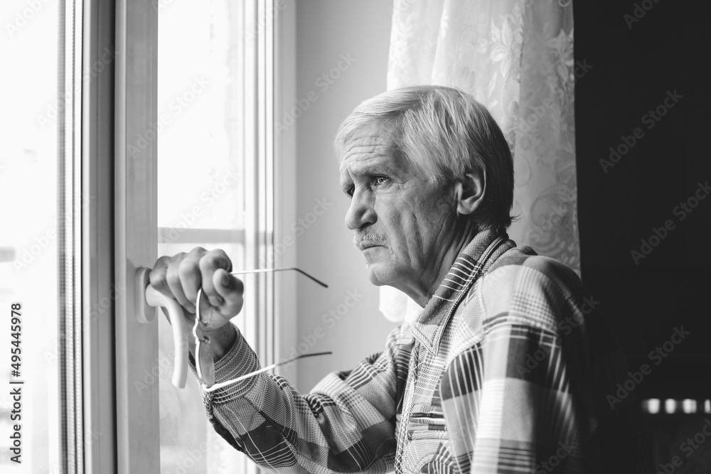 Side view of older man holding eyeglasses standing by the window in ...