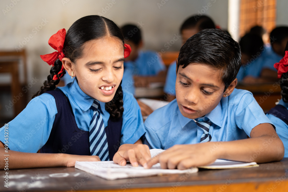 Focus on girl, kid helping his friend for studying at classroom ...