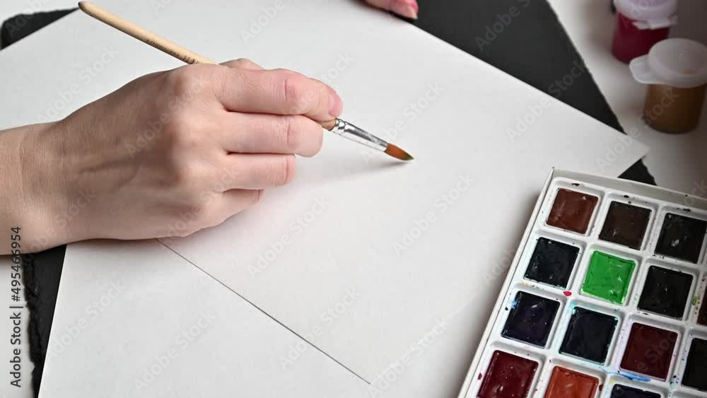 Female artist hands painting with watercolor paints on white piece of ...