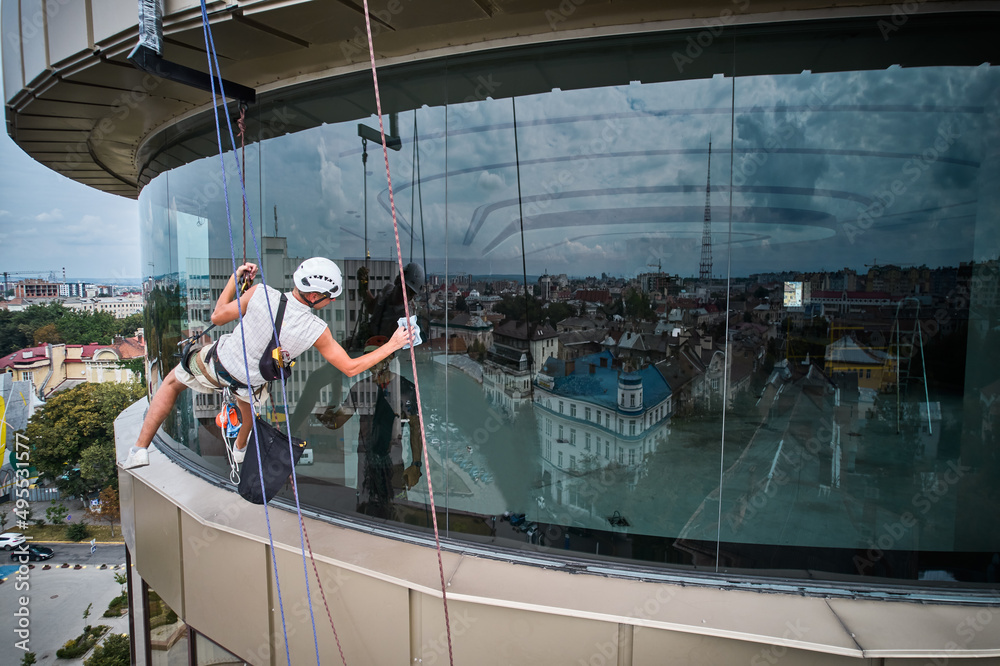 Industrial mountaineering worker cleaning window of high-rise building ...