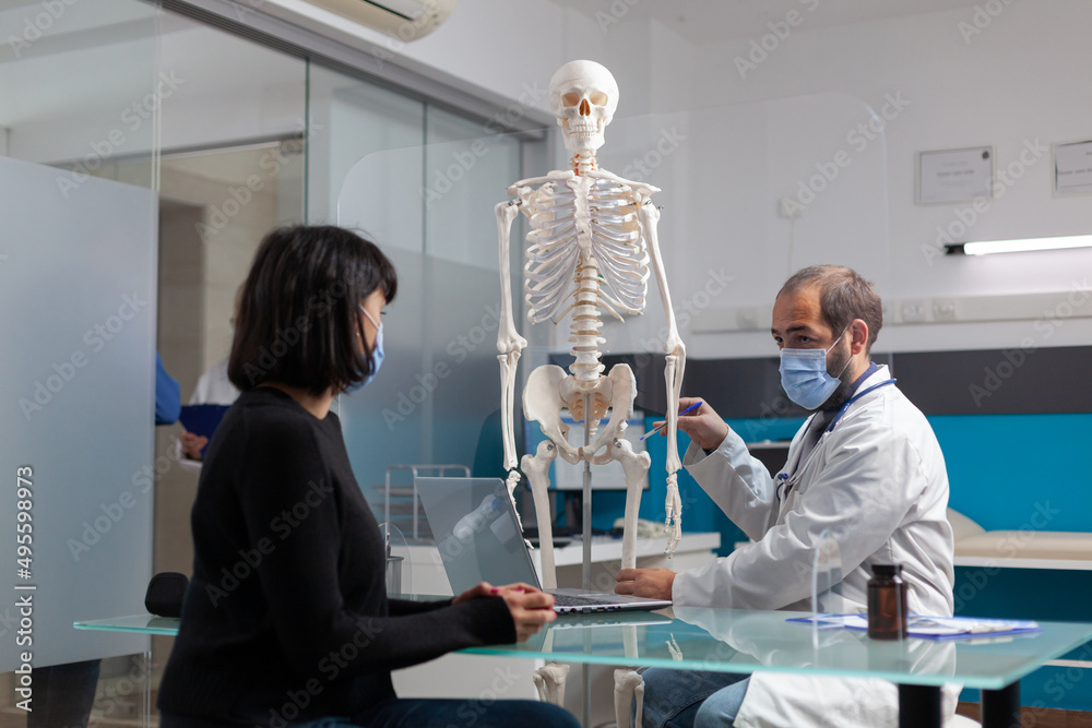 Physiotherapist showing joint on human skeleton to woman in cabinet ...