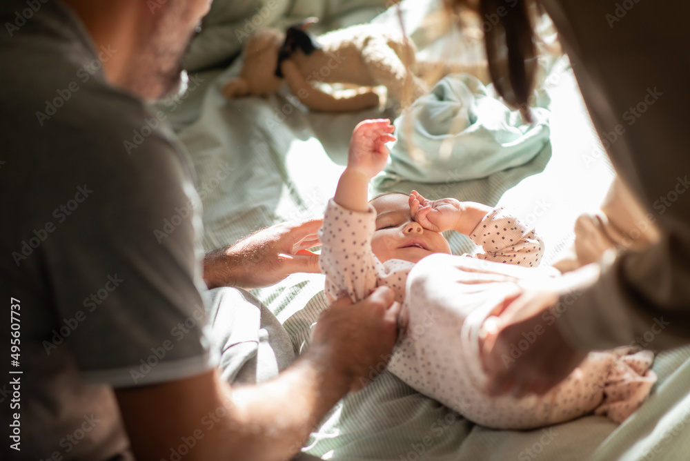 Parents dressing baby boy together in bedroom. Happy little child lying ...