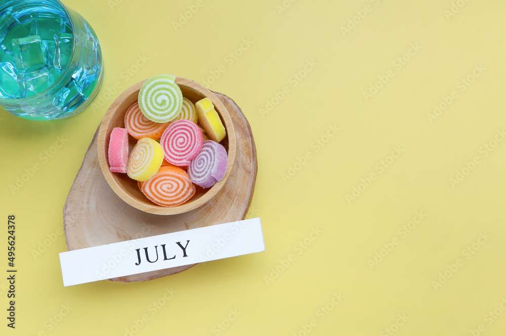 Hello July, July text on white wood block and jelly sweet on yellow ...