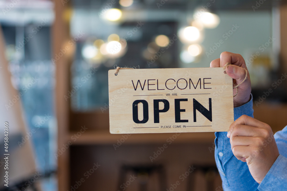 The owner holds a sign, opens the door and is ready to serve the young ...