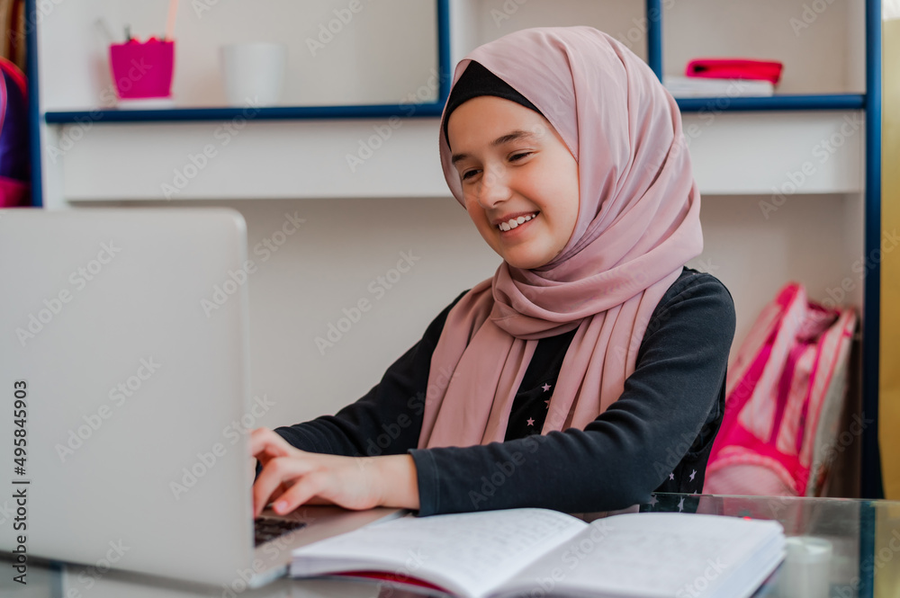 Muslim girl student in hijab smiling while learning for school at home ...