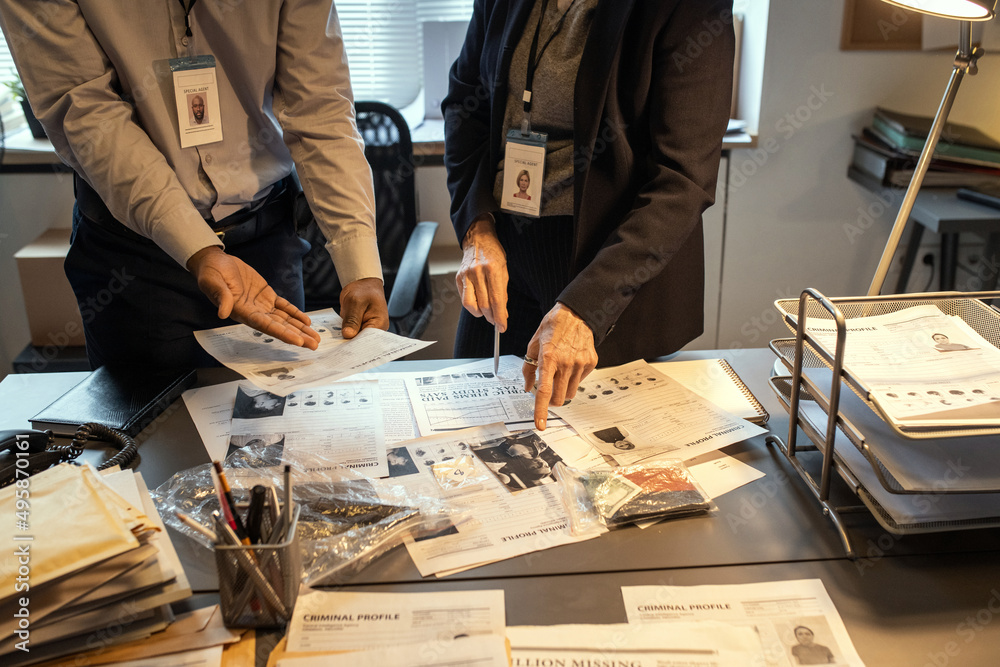 Hands of intercultural agents of FBI discussing criminal profiles by ...