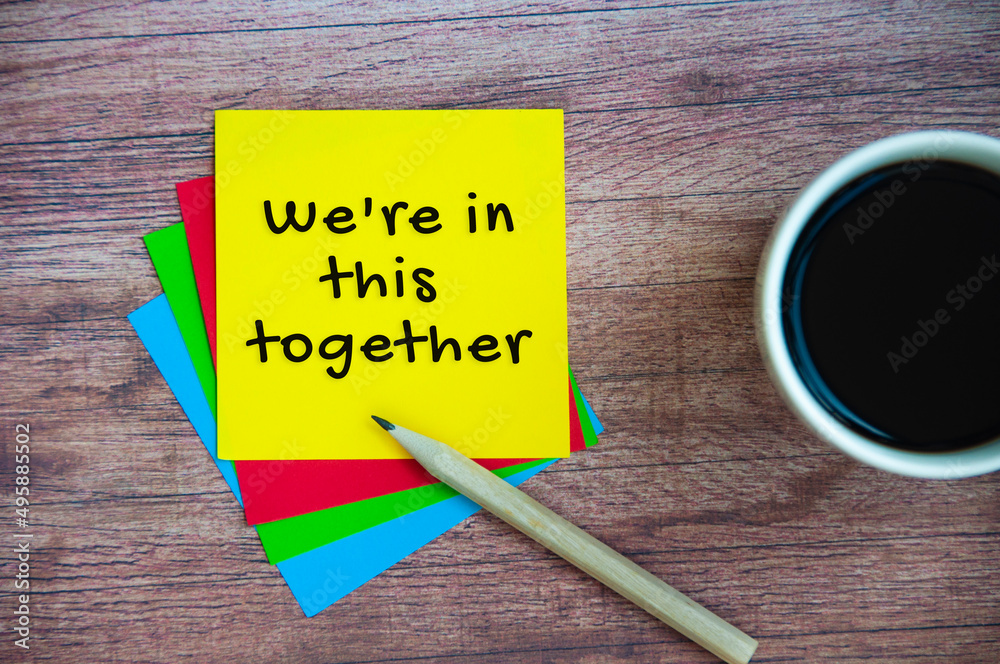 We are in this together text on yellow notepad with coffee, pencil and ...