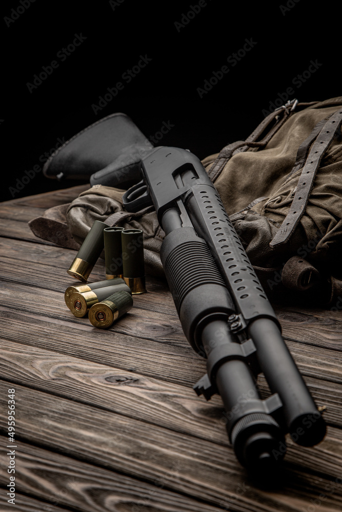 A black 12-gauge pump-action shotgun and ammo are on a canvas backpack ...