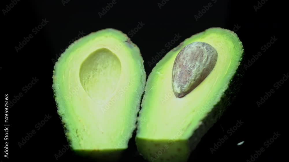 Two halves of an avocado rotate in a circle on a black background. A ...