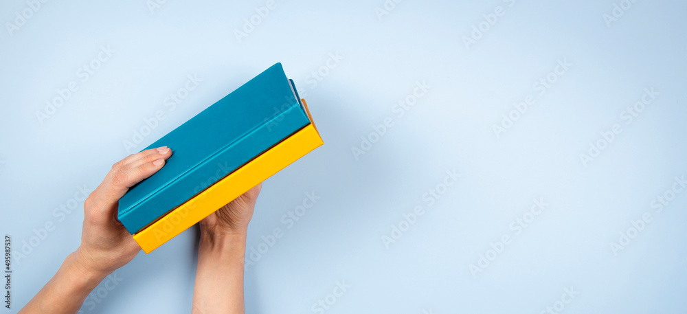 Female hands holding two blue and yellow color books over light blue ...