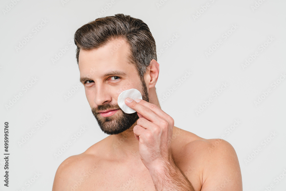 Caucasian shirtless young man using cotton pad for applying removing ...