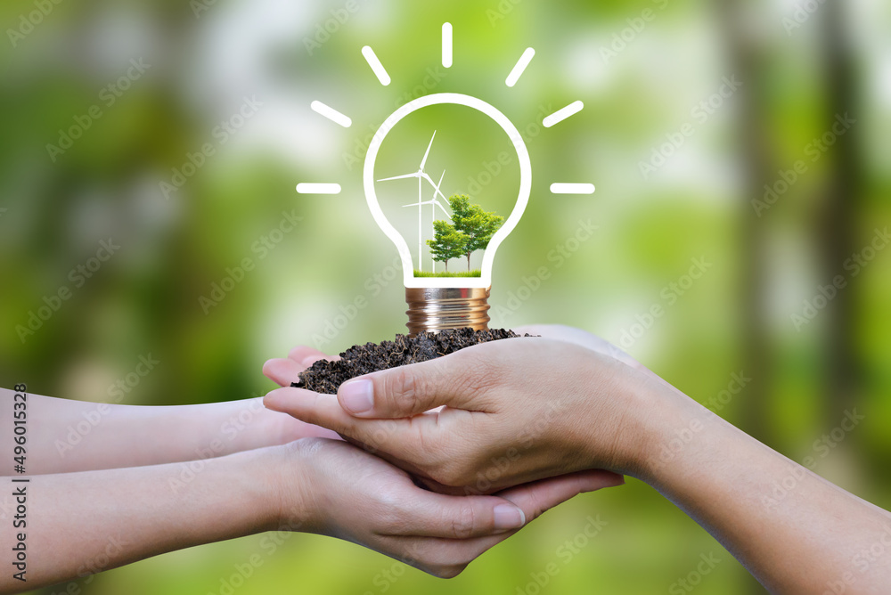 Two people holding light bulb with tree and windmill on green ...