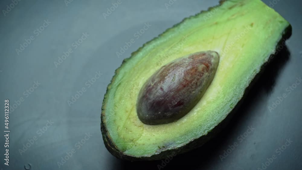 Half of an avocado with a stone rotates in a circle on a black ...