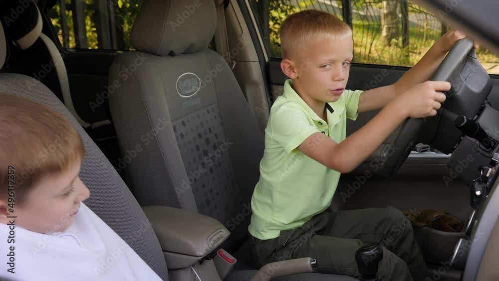 Two cheerful boys of eight years old are sitting behind the wheel of a ...