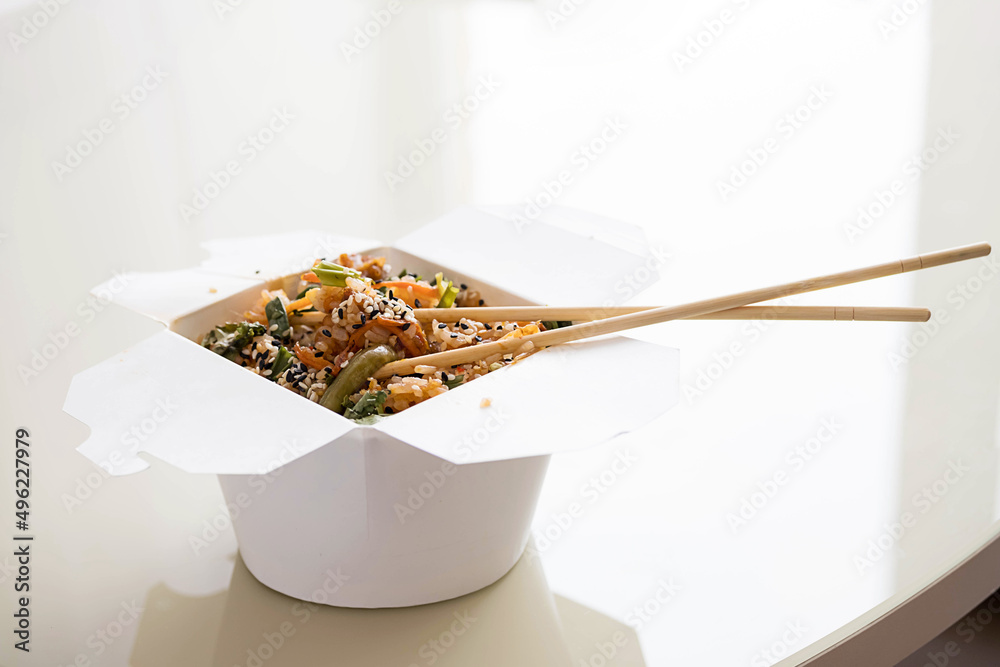 Rice with pork and vegetables in take-out box with chopsticks on table ...