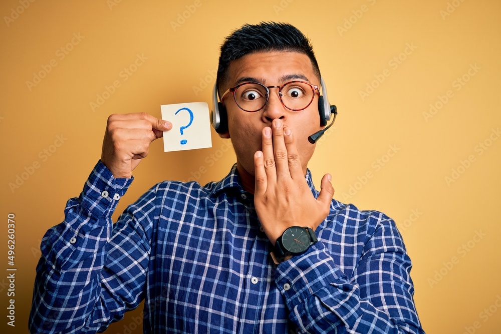 Young latin call center agent man holding question mark reminder paper ...