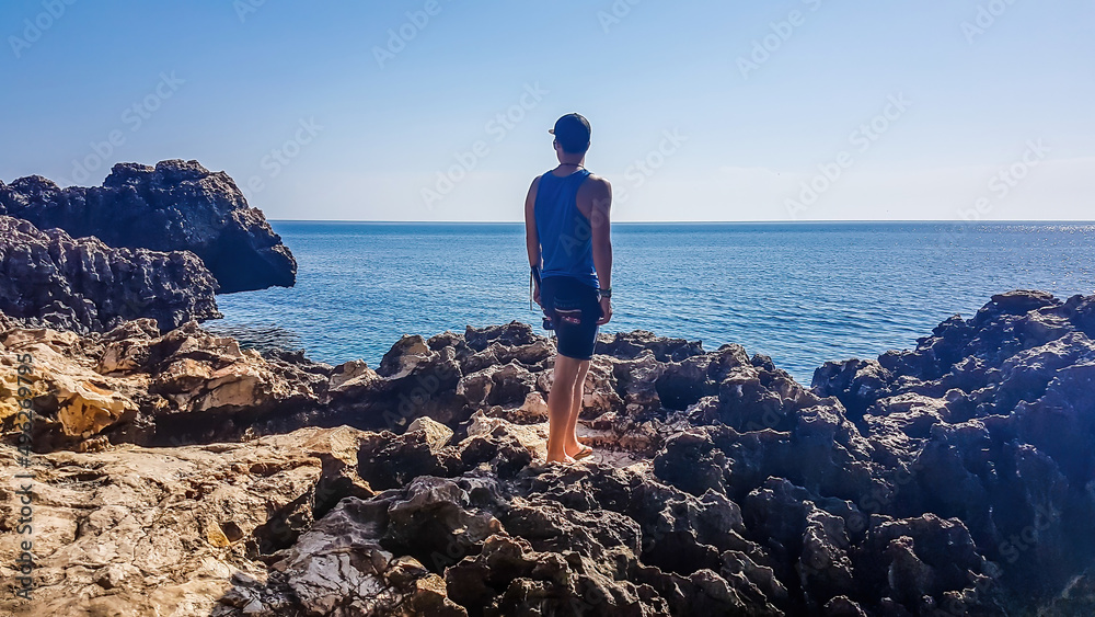 Young man standing in between the steep cliffs of Cape Greco, Cyprus ...