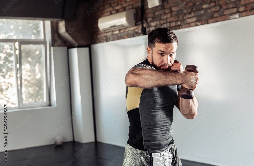 Athletic male fighter trains punches with dumbbells in a sports hall ...