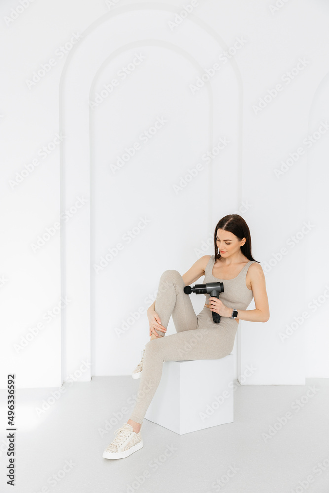 A girl in a tracksuit massaging with a vibrating massager. An electric ...