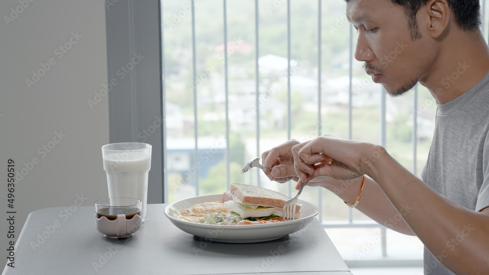 Asian young man eating breakfast at the dining room table full of food ...