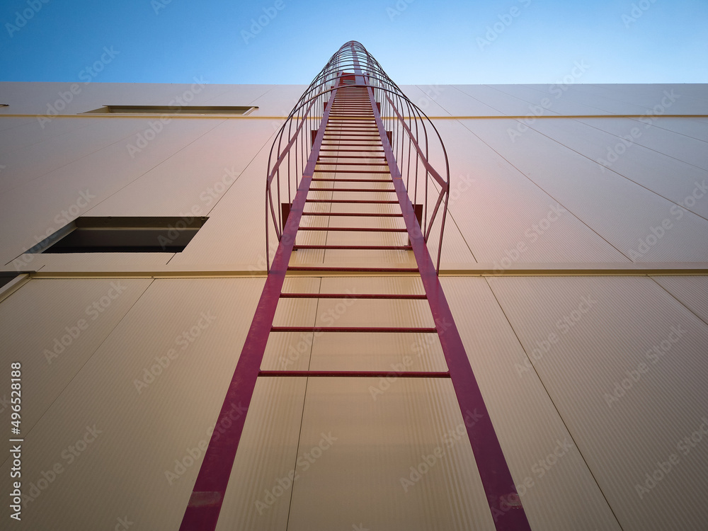 Outdoor fire escape ladder on industrial building wall. Bottom up view ...