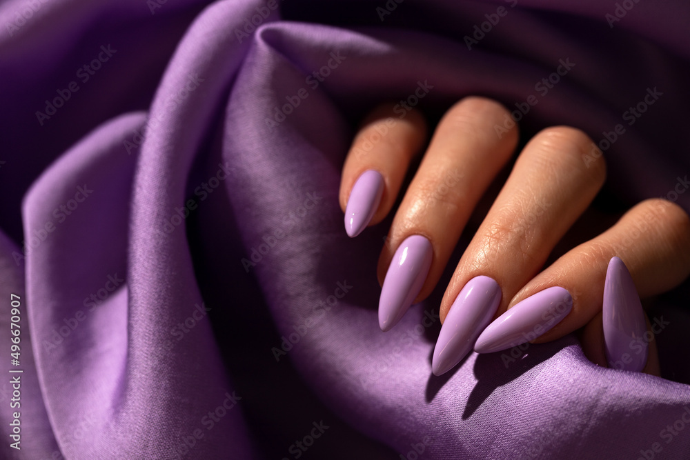 Girl's hand with an elegant manicure in a purple color on a purple silk ...