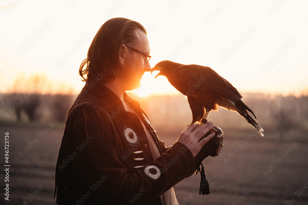 Man and wild bird over sunset sky looking on each other Buzzard or ...