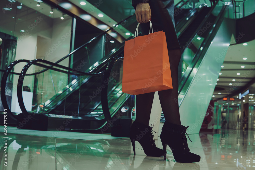 Toned shot of woman in black wearing heels walking with red paper bag ...