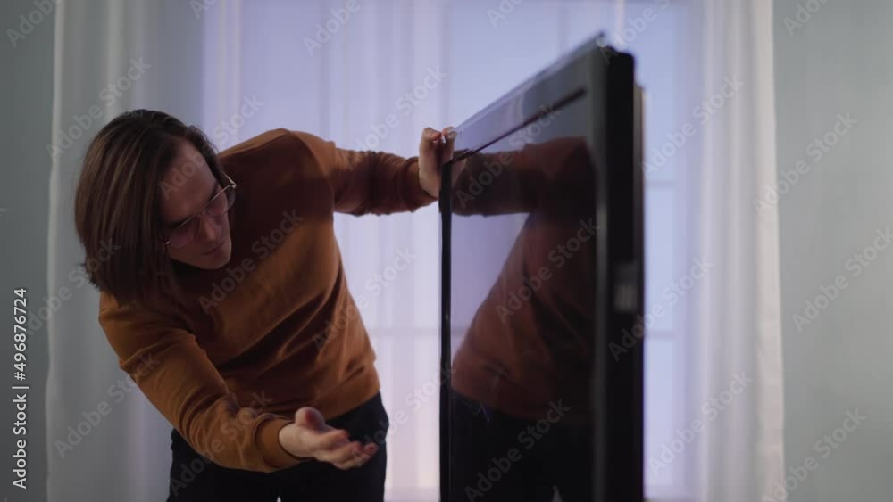 Confused man slams smart TV screen with trenches against window ...
