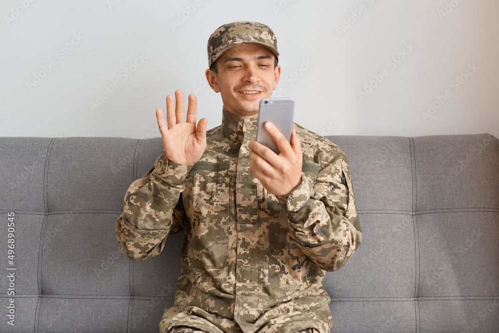 Image of happy military man wearing camouflage uniform sitting on sofa ...
