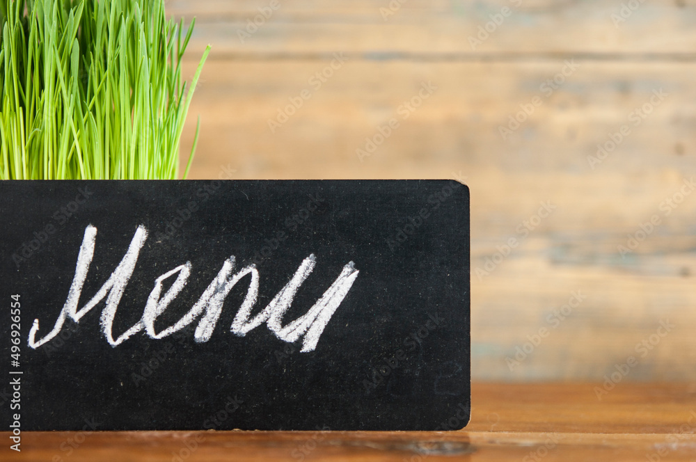 Menu written with chalk on aged blackboard over spring grass background ...