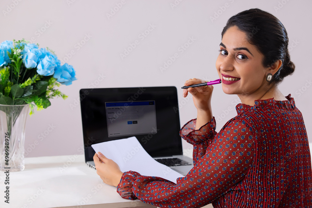 Portrait of a working woman looking back at camera while working at her ...