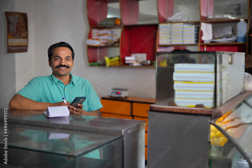 Portrait of Sweet shop owner maintaining accounts by using Smartphone ...