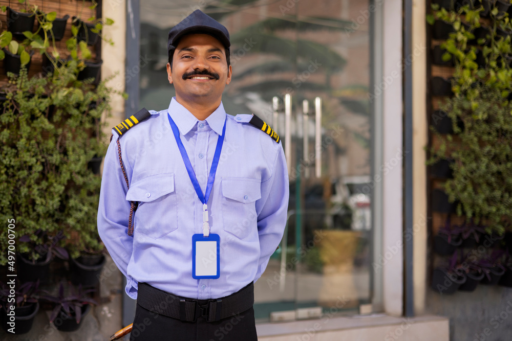 Portrait of security guard with hands behind back while working at gate ...