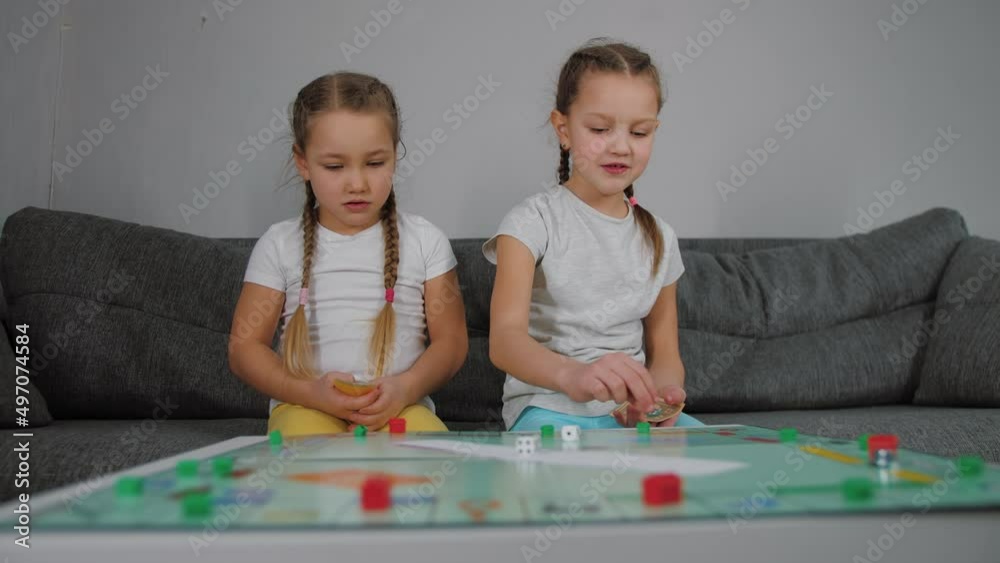 Two little girls playing tabletop game, sitting on sofa. Caucasian cute ...