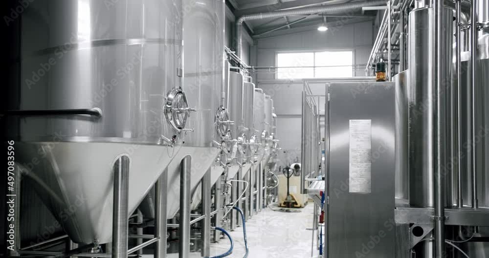 Panning shot of rows of large steel tanks with beer in industrial ...