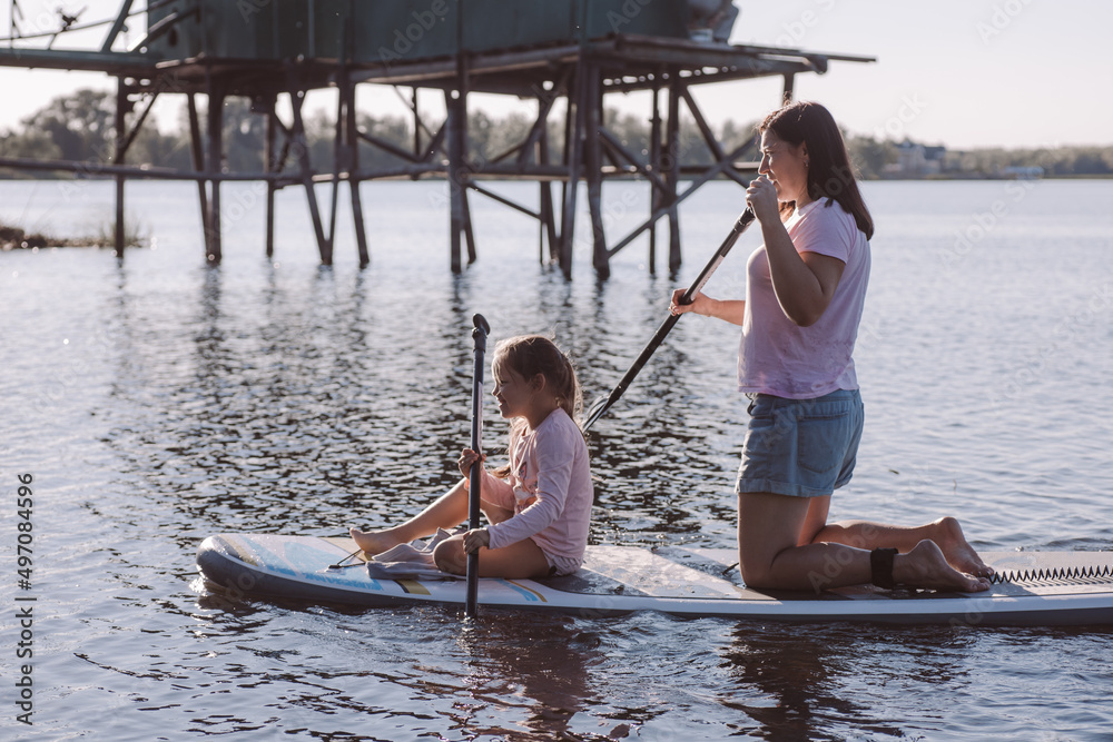 Little girl with mother sup boarding together on one sup in daytime ...