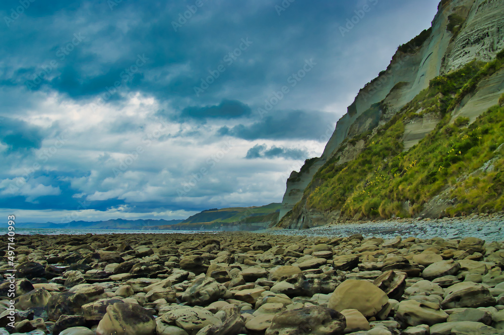 Rocky beach, steep limestone cliffs and a dark, threatening sky at ...