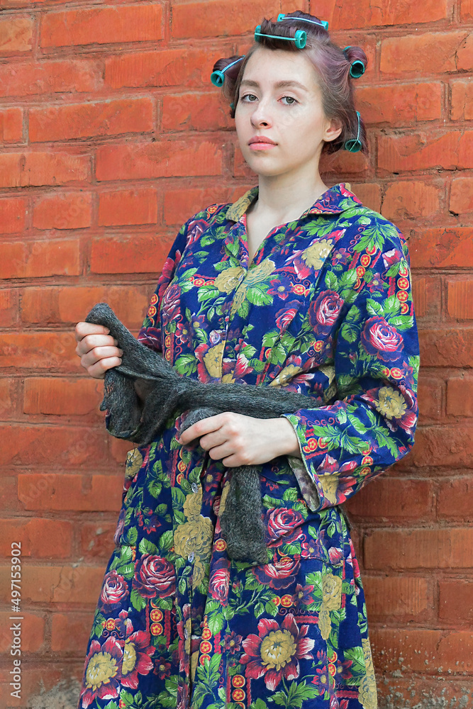 A young beautiful girl stands leaning on a brick wall, she is dressed ...