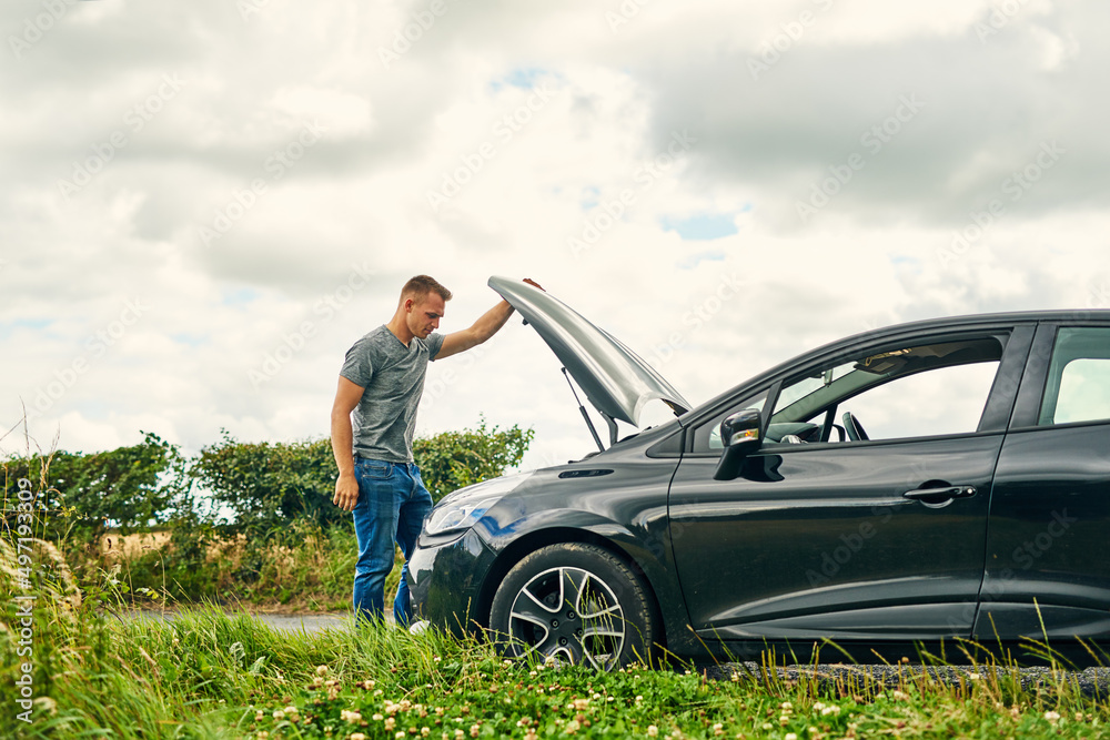 Nobody wants their journey cut short by car problems. Shot of a young man checking under the ...