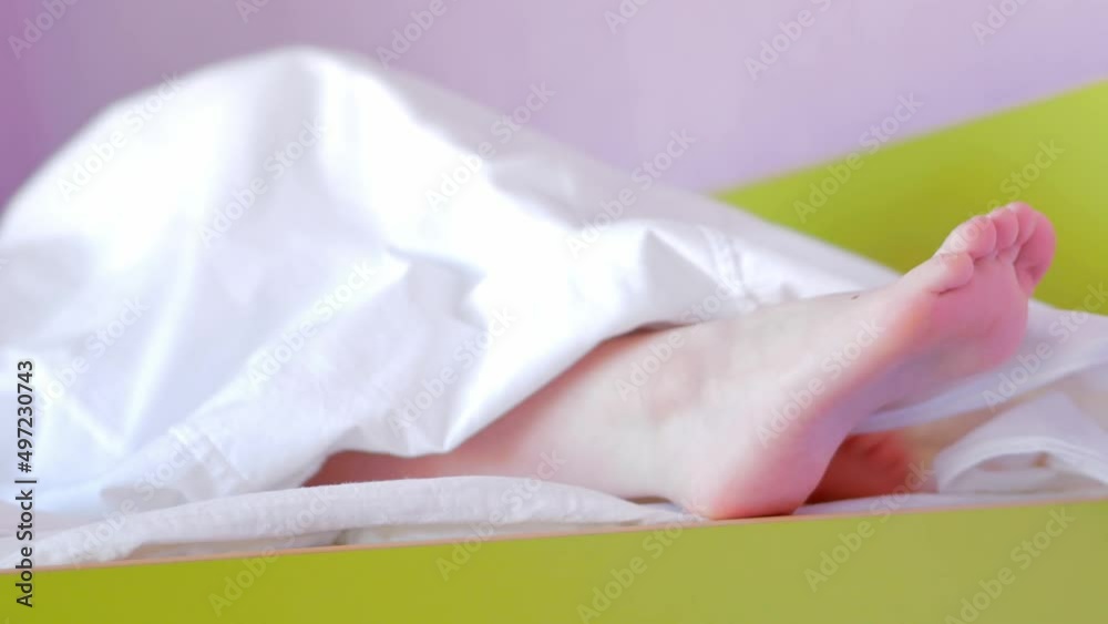 Bare feet of a baby close-up on a white bed in a green crib. The kid is ...