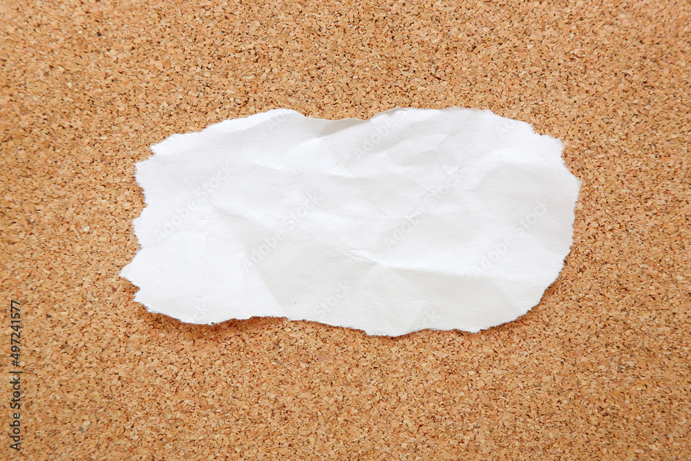 A piece of white crumpled paper with uneven edges on a cork board ...