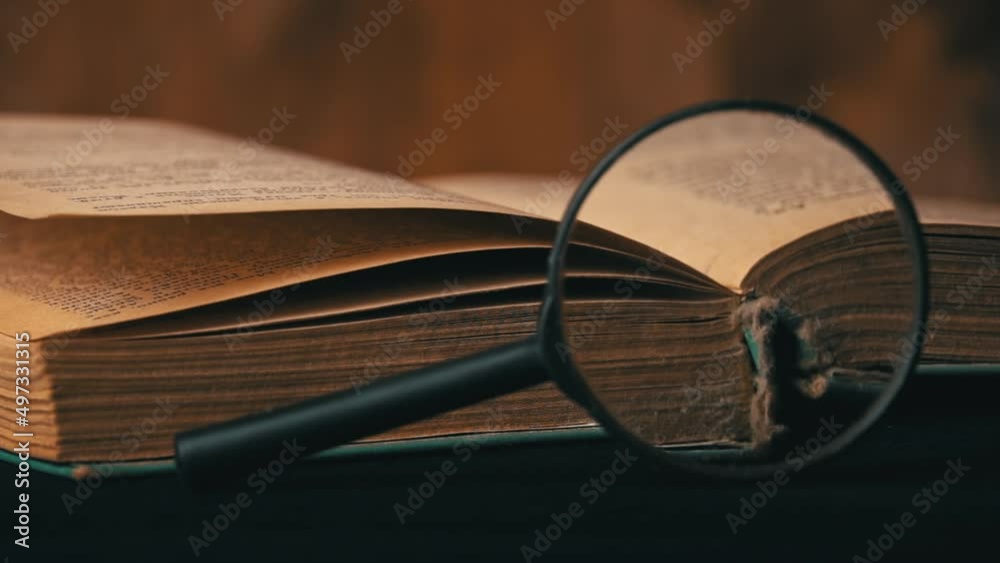 The pages of an old book are turning next to a magnifying glass. A ...
